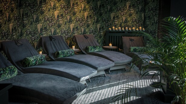 Uma área de spa com três cadeiras reclináveis, uma parede com padrão de folhagem e uma fileira de velas.