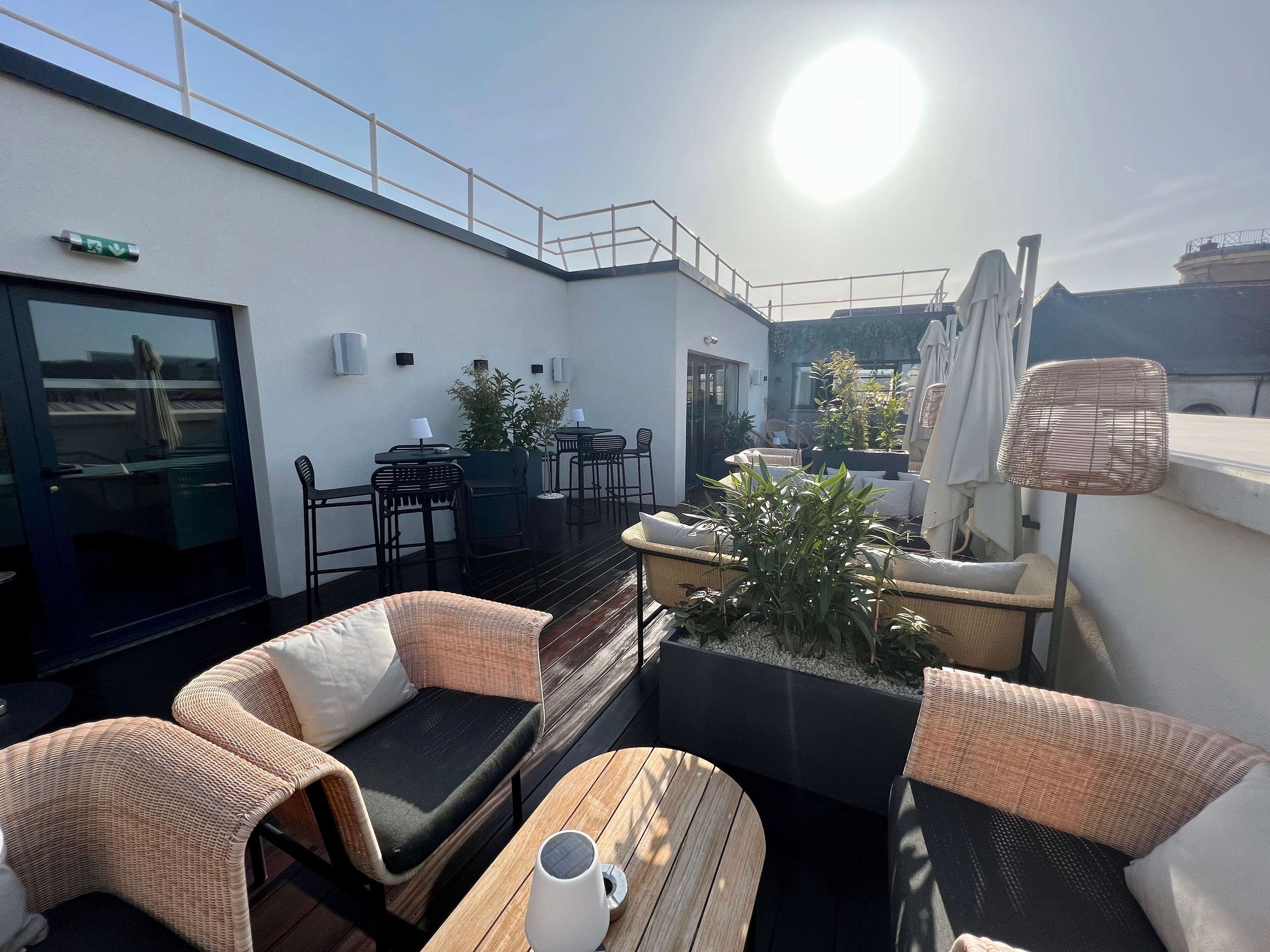Terraço no telhado com móveis de vime, uma mesa de centro e plantas em vasos.