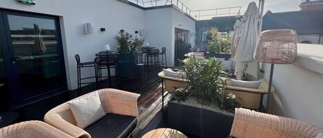Terraço no telhado com móveis de vime, uma mesa de centro e plantas em vasos.