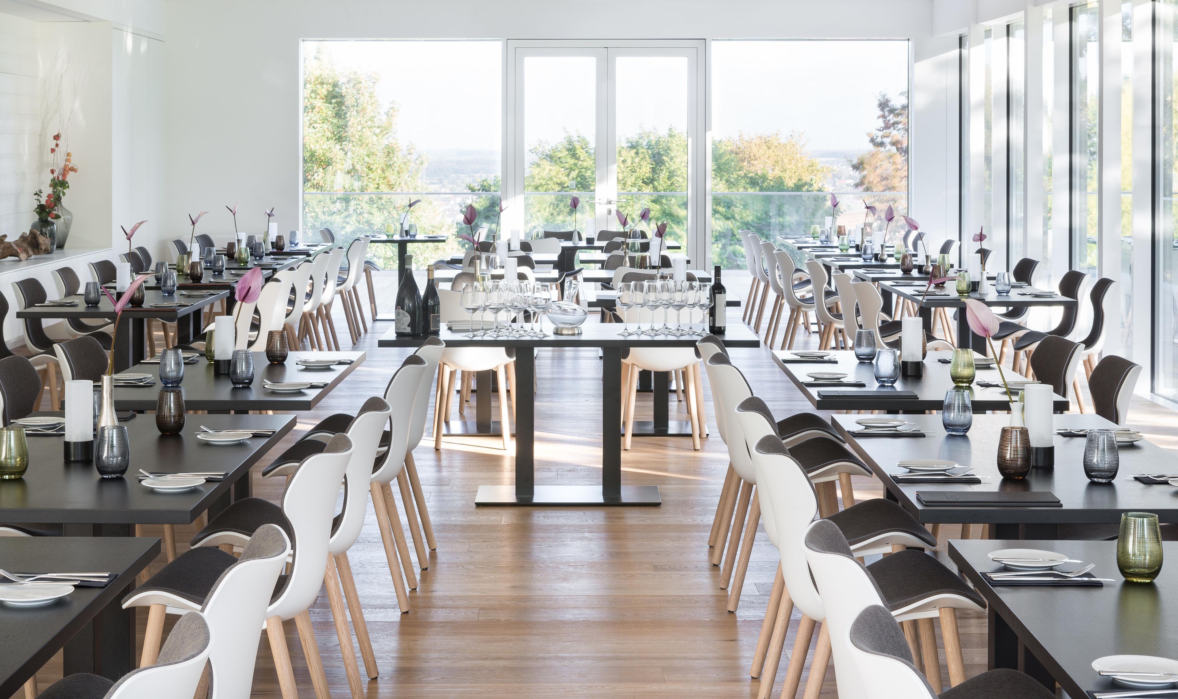 Uma ampla sala de jantar com várias mesas e cadeiras, grandes janelas com vista para o exterior e um design de interiores moderno.