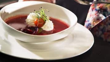 Uma tigela branca de sopa com um pouco de creme e enfeites sobre um prato branco.