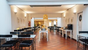 Uma ampla sala de jantar com várias mesas e cadeiras, uma mesa central para servir e iluminação suspensa.