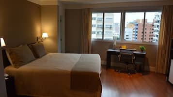 Quarto de hotel com uma cama grande, uma escrivaninha com cadeira e uma janela com vista para a cidade.