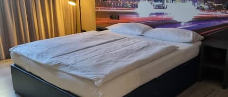 Quarto de hotel moderno com cama grande, painel com céu noturno, luminária e vista para a cidade.