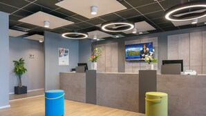 Uma área de recepção com design moderno, incluindo um balcão de atendimento, uma tela de televisão e um vaso de planta.