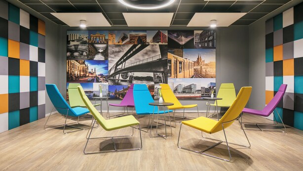 Uma área de espera moderna com cadeiras coloridas e um mural com vista para a cidade.