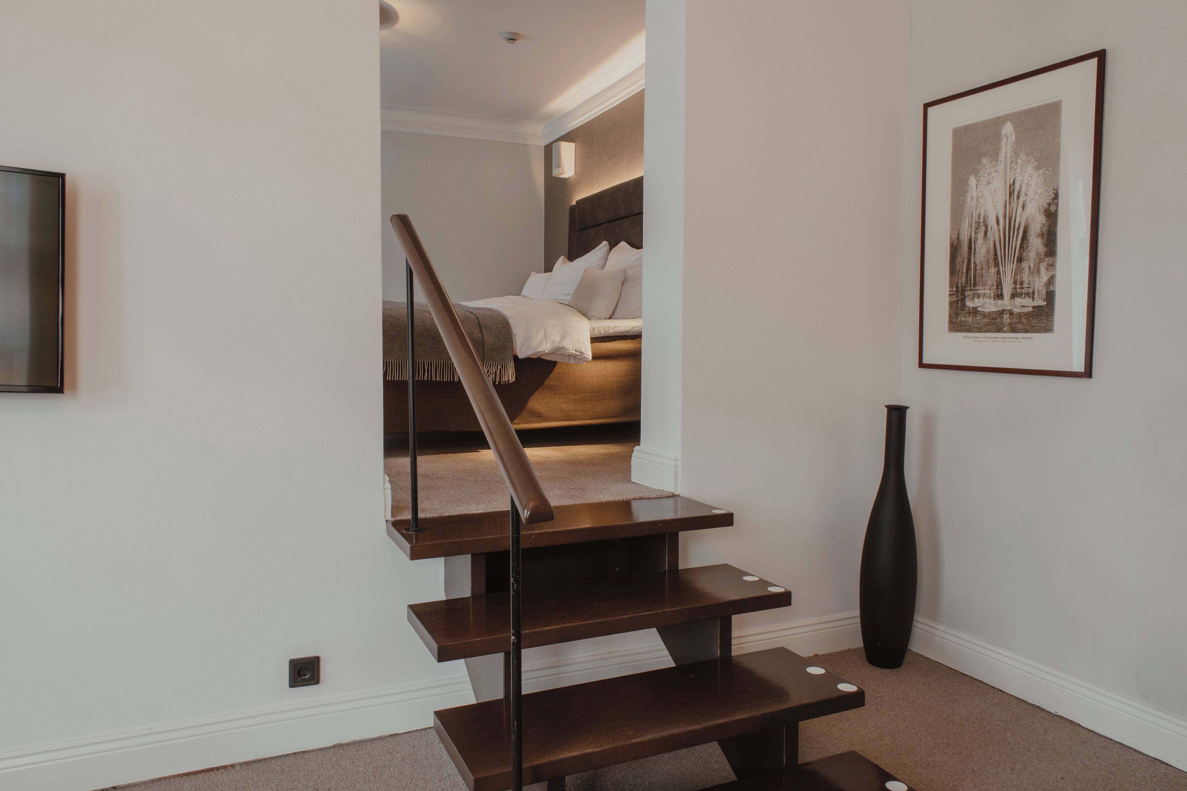 Uma escadaria que leva a um quarto com uma cama, um quadro emoldurado e um vaso.