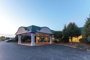 Entrada de hotel com área de estacionamento coberta e um edifício com telhado verde.