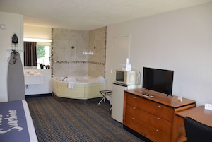 Quarto de hotel com cama, cómoda de madeira, televisão, micro-ondas, pia e banheira.