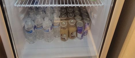 Geladeira repleta de bebidas variadas, incluindo refrigerantes, água e café.