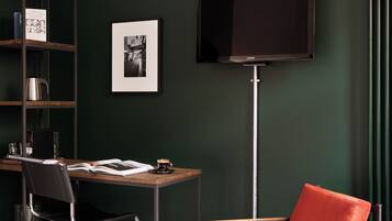Quarto moderno com escrivaninha, cadeira, estante de livros, quadro emoldurado e televisão de tela plana fixada na parede.
