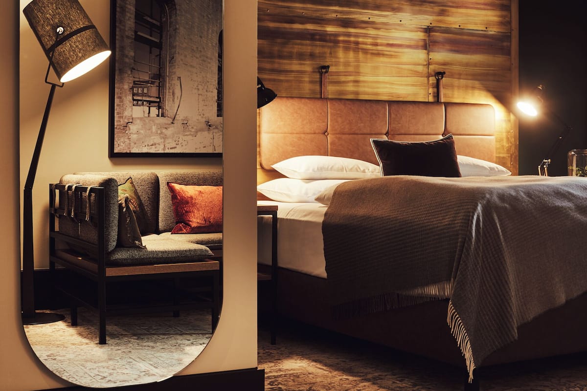 Quarto moderno com cama, sofá, luminária e um quadro na parede.