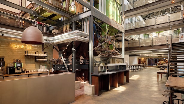 Um interior em estilo industrial com dutos aparentes, um bar de café e um mezanino.