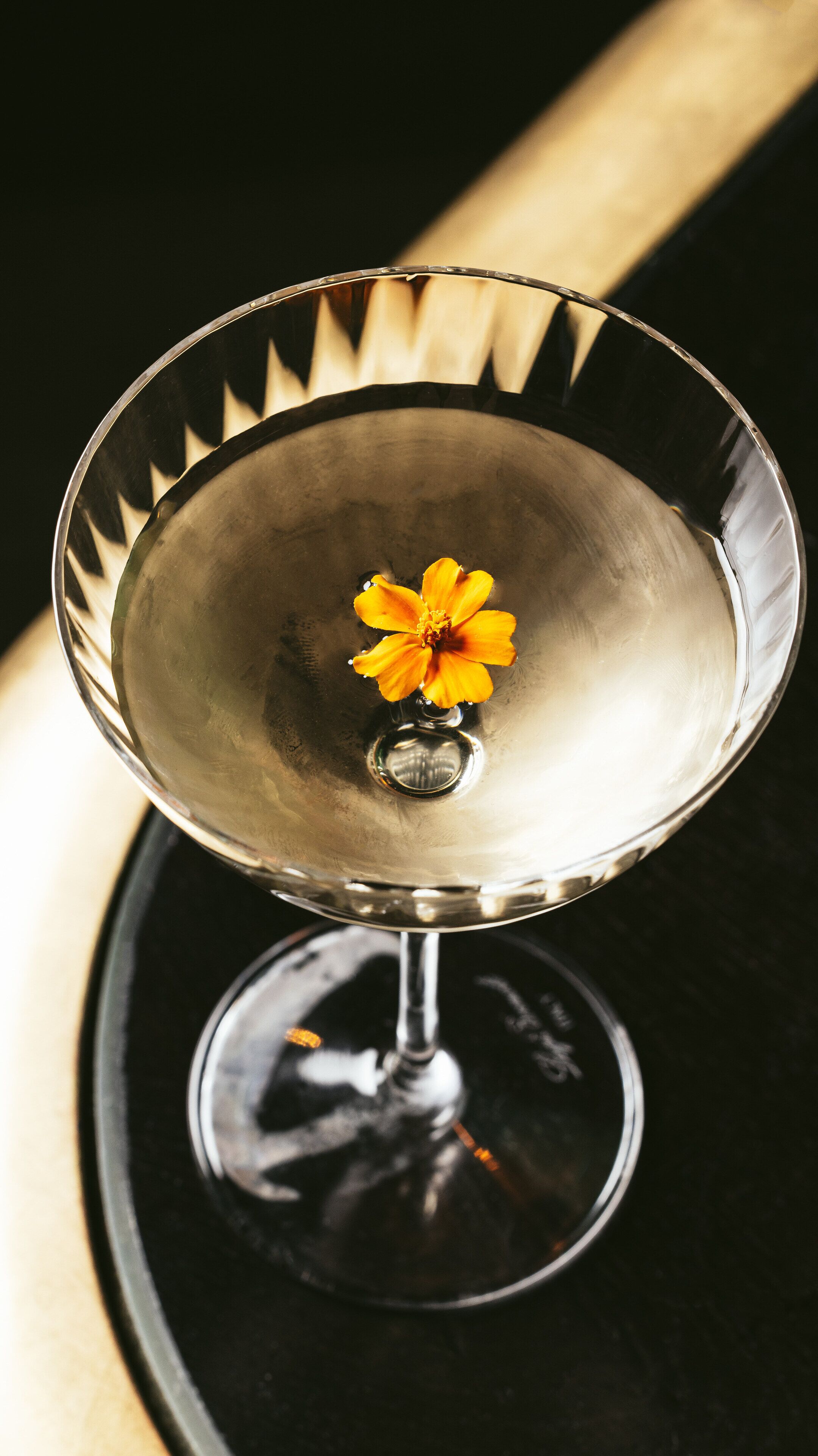 Taça martini de vidro transparente com uma flor sobre uma superfície refletora.
