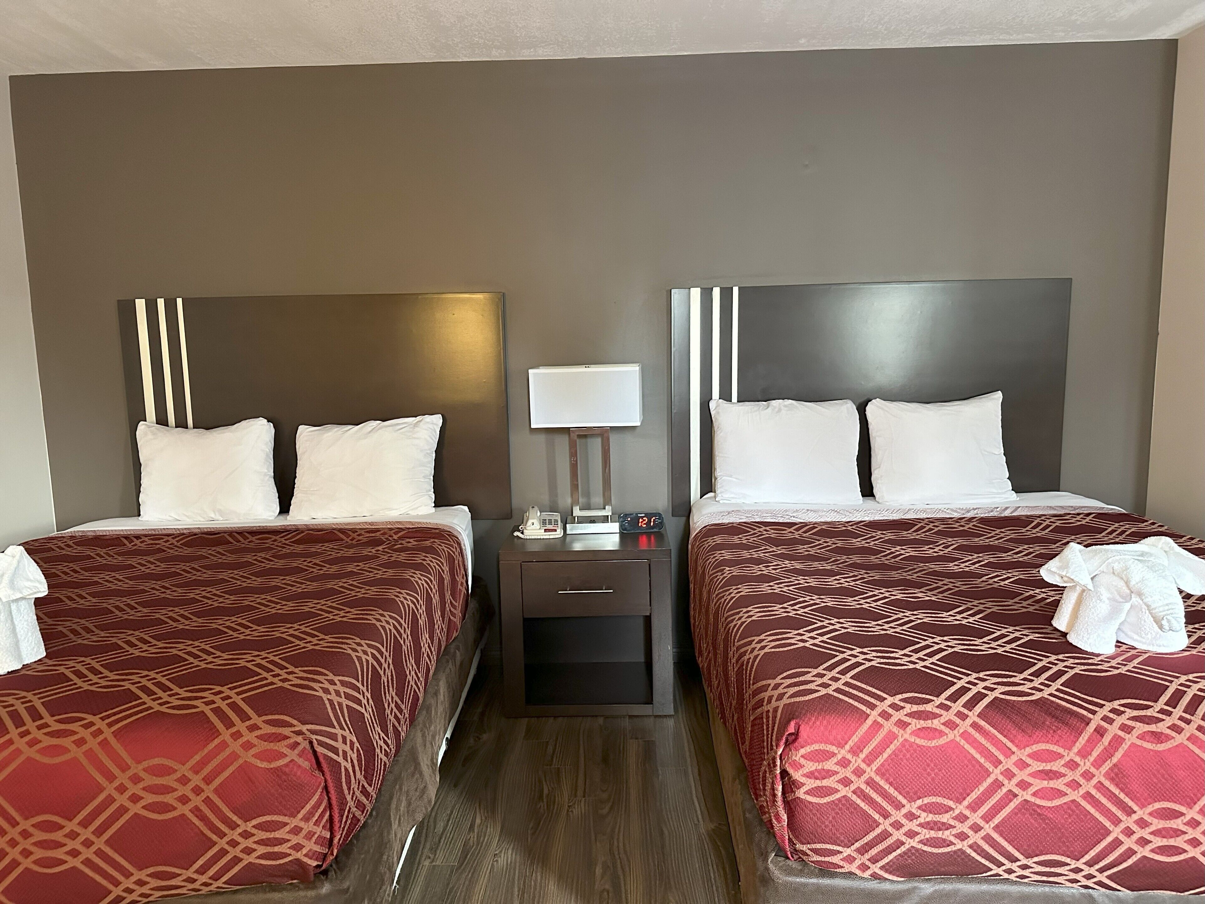 Quarto de hotel com duas camas, cada uma com colcha estampada, mesa de cabeceira com abajur e relógio.