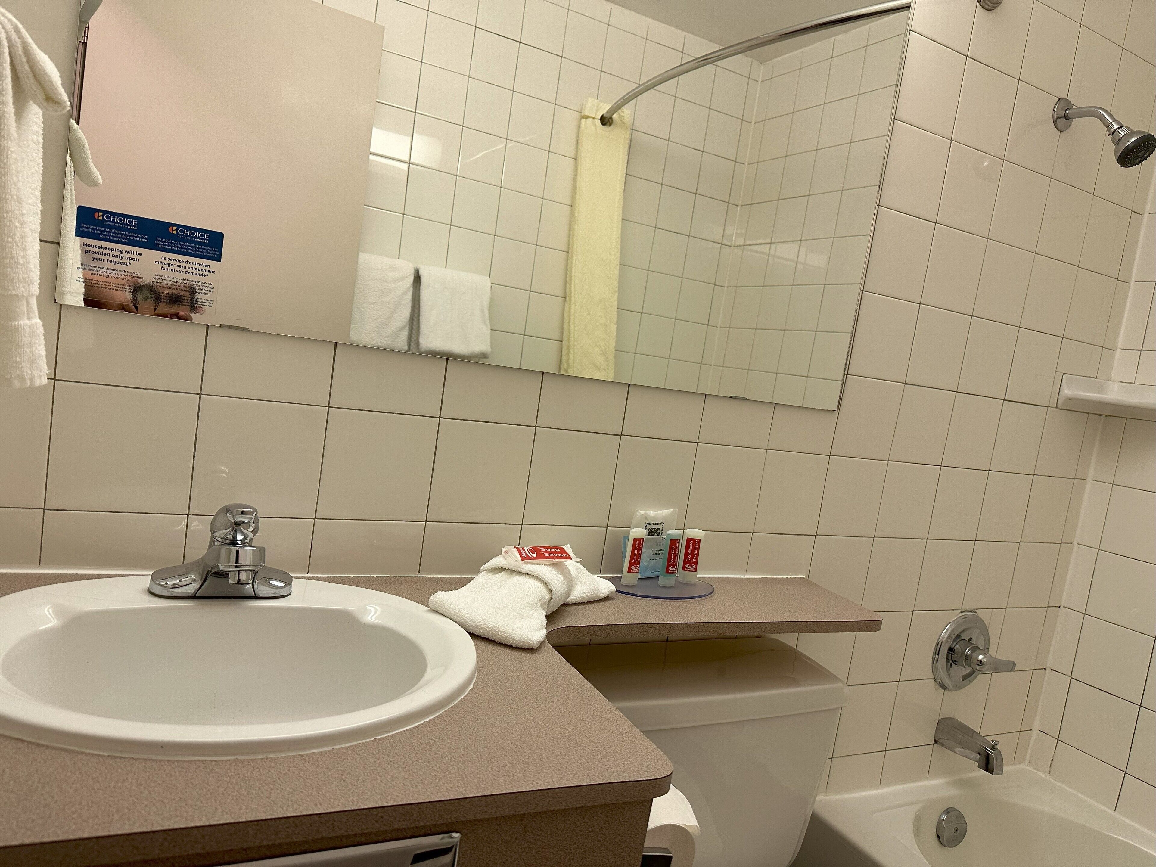 Casa de banho com lavatório, espelho e chuveiro. Inclui um porta-toalhas e uma pequena prateleira com produtos de higiene pessoal.
