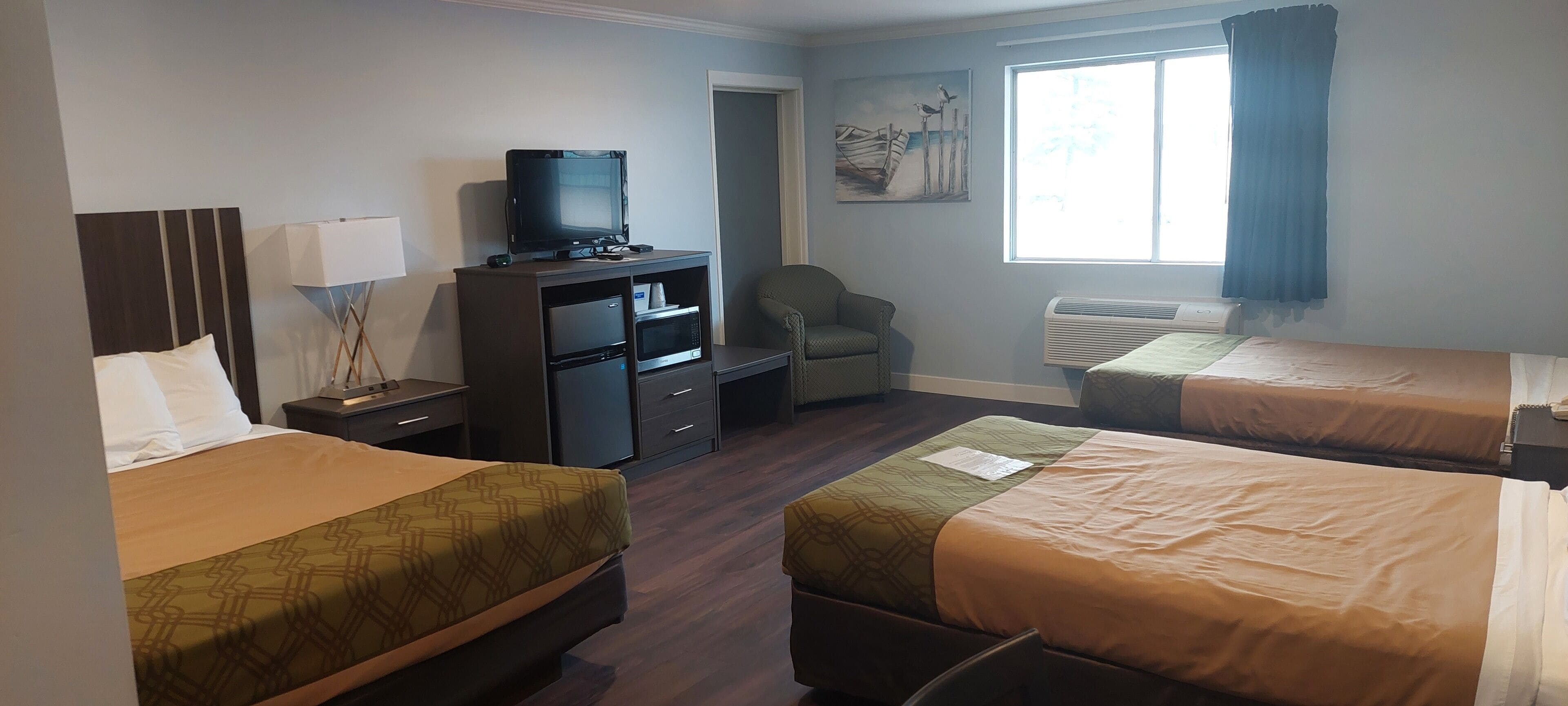 Quarto de hotel com duas camas, uma televisão sobre uma cômoda, uma escrivaninha com luminária, uma cadeira e uma janela com vista para barcos.