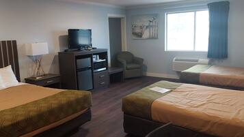 Quarto de hotel com duas camas, uma televisão sobre uma cômoda, uma escrivaninha com luminária, uma cadeira e uma janela com vista para barcos.