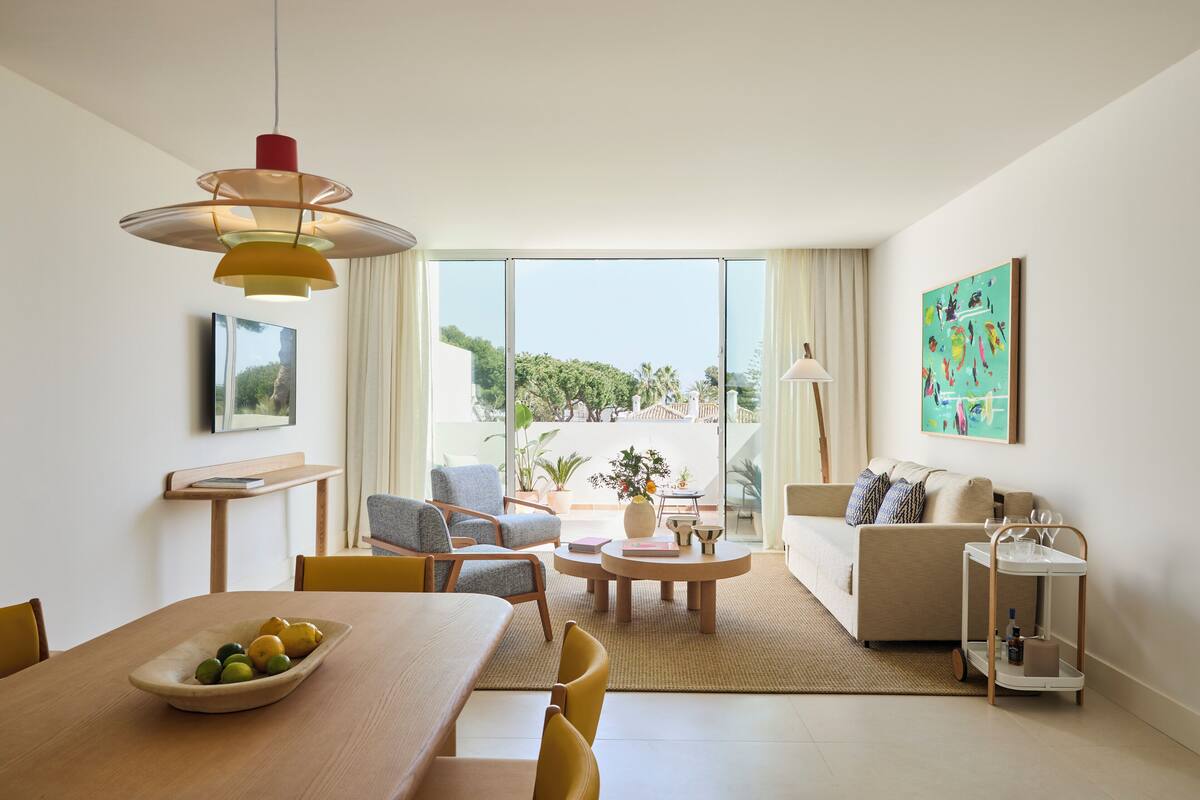 Uma sala de estar moderna com área de jantar, janelas amplas e vista para o verde lá fora.