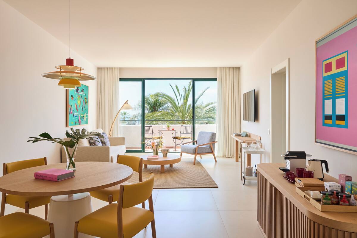 Quarto de hotel moderno com área de refeições, varanda e vista, além de um balcão de recepção.