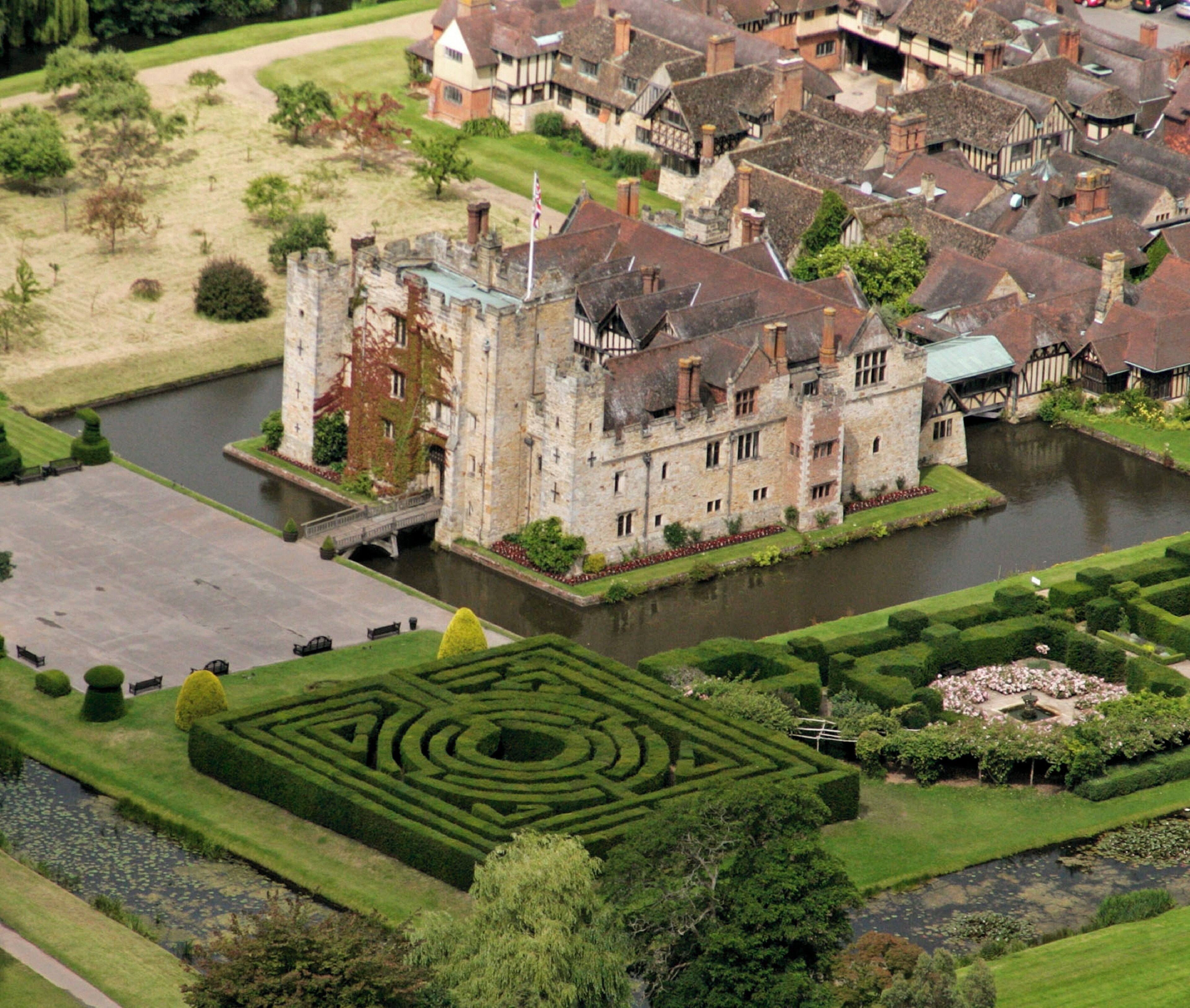 Um castelo rodeado por um jardim formal e uma pequena ponte, com um fosso.