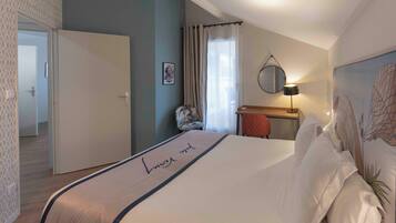 Quarto de hotel com cama, escrivaninha, cadeira, janela com cortinas e um quadro pendurado na parede.