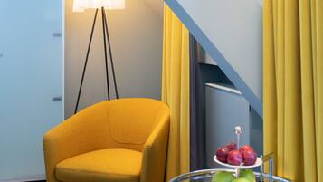 Uma sala de estar moderna com uma poltrona amarela, um abajur, uma mesa de vidro com frutas e uma escada com cortinas amarelas.