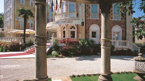 Entrada de hotel com arco de pedra, caminho pavimentado e jardim bem cuidado.