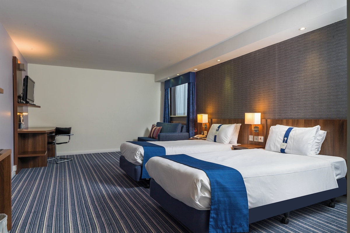 Quarto de hotel com duas camas, uma escrivaninha e uma cadeira.
