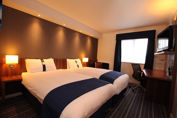 Quarto de hotel com duas camas, uma mesa e uma cadeira.