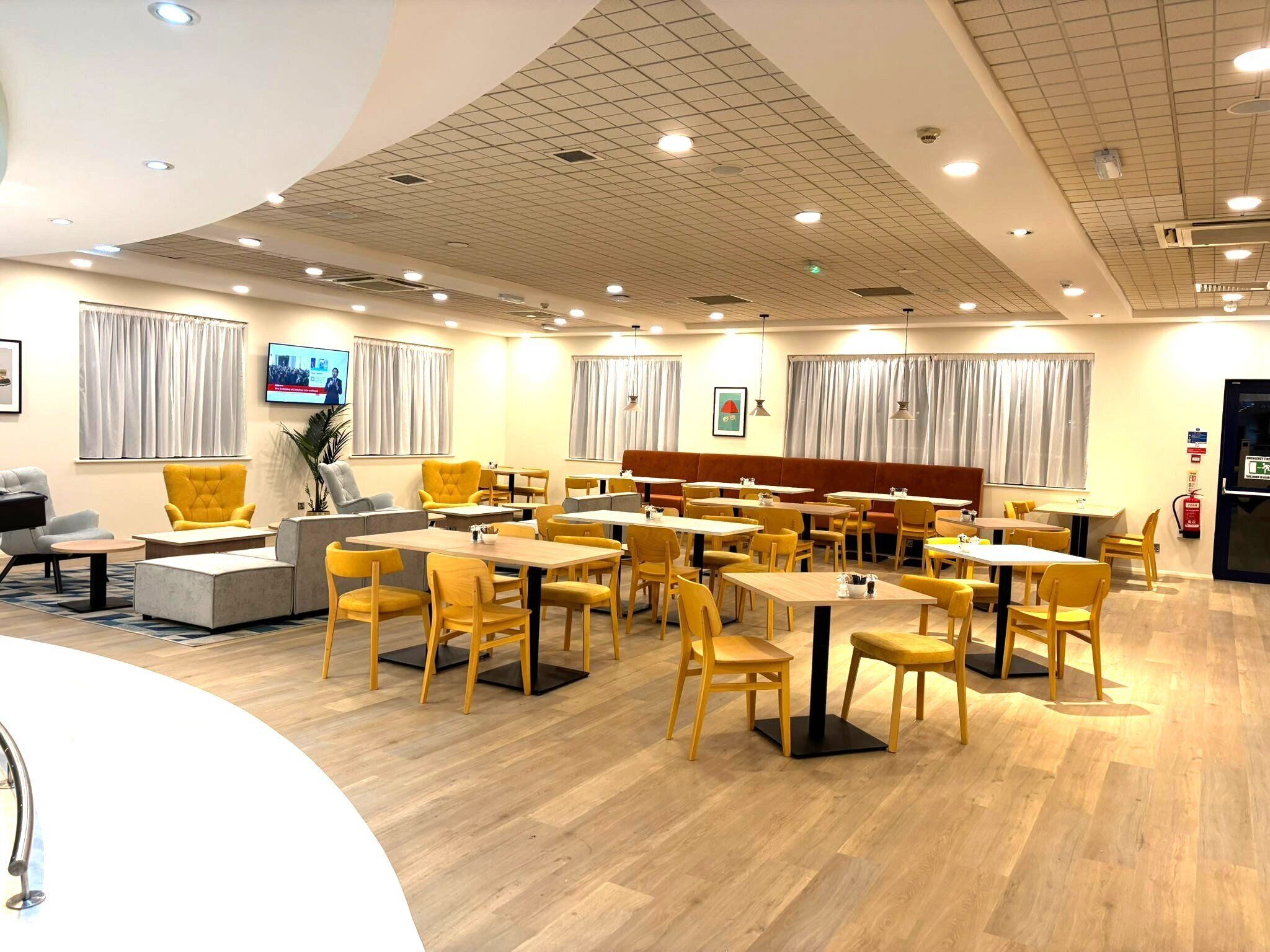 Uma sala de jantar moderna com várias mesas e cadeiras, um sofá e uma televisão.