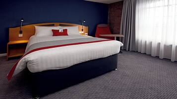 Quarto de hotel com uma cama grande, uma cadeira vermelha, cabeceira de madeira e parede de tijolos.