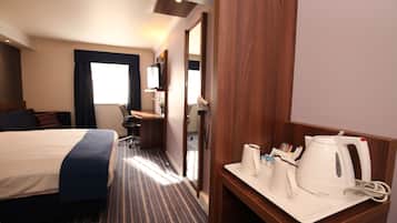 Quarto de hotel com cama, escrivaninha, cadeira, cafeteira e telefone.