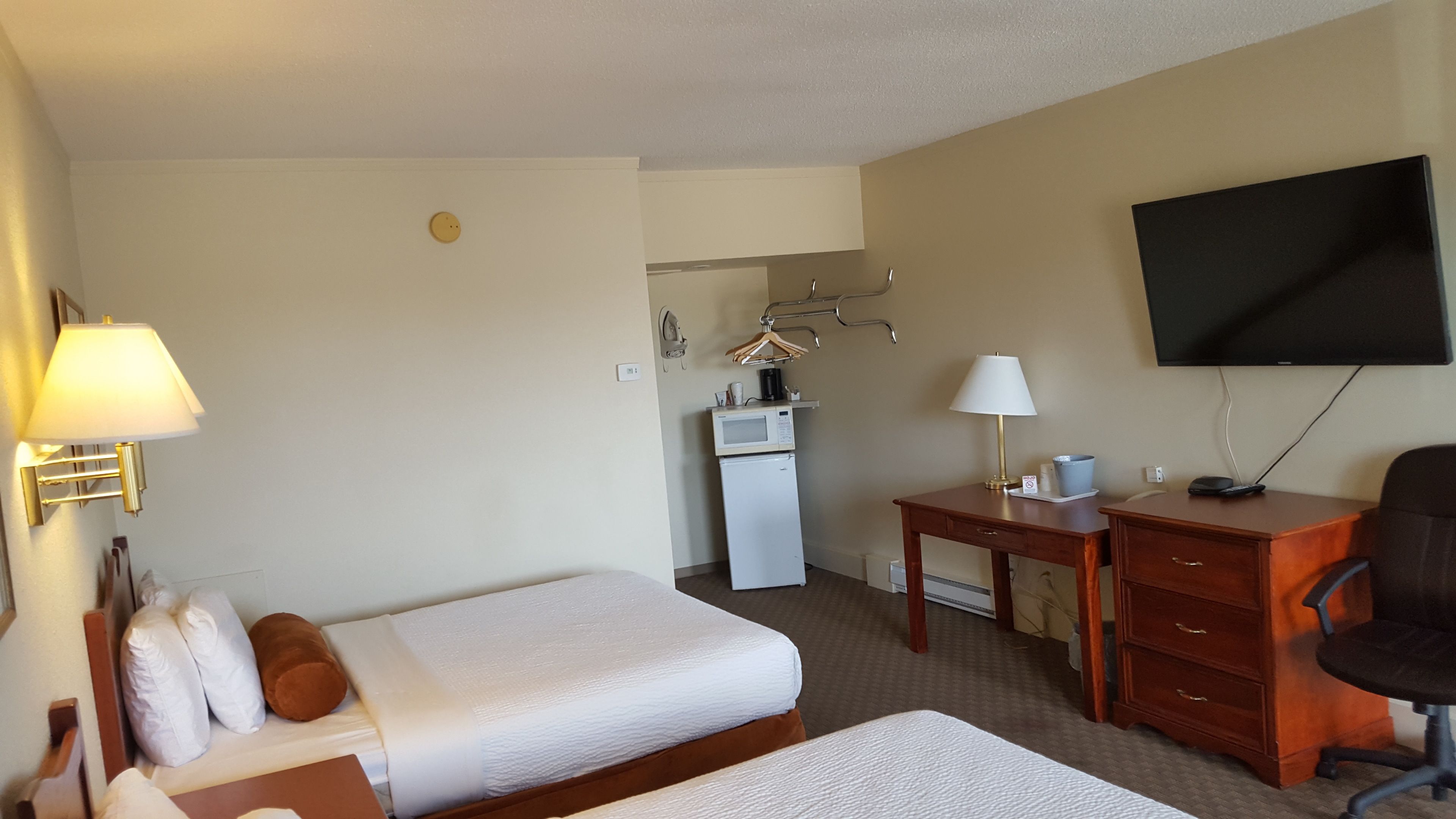 Quarto de hotel com cama, escrivaninha, cadeira, televisão e cozinha compacta.