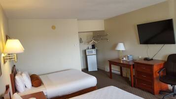 Quarto de hotel com cama, escrivaninha, cadeira, televisão e cozinha compacta.