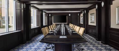 Uma sala de conferências com uma mesa comprida, cadeiras e uma tela grande.
