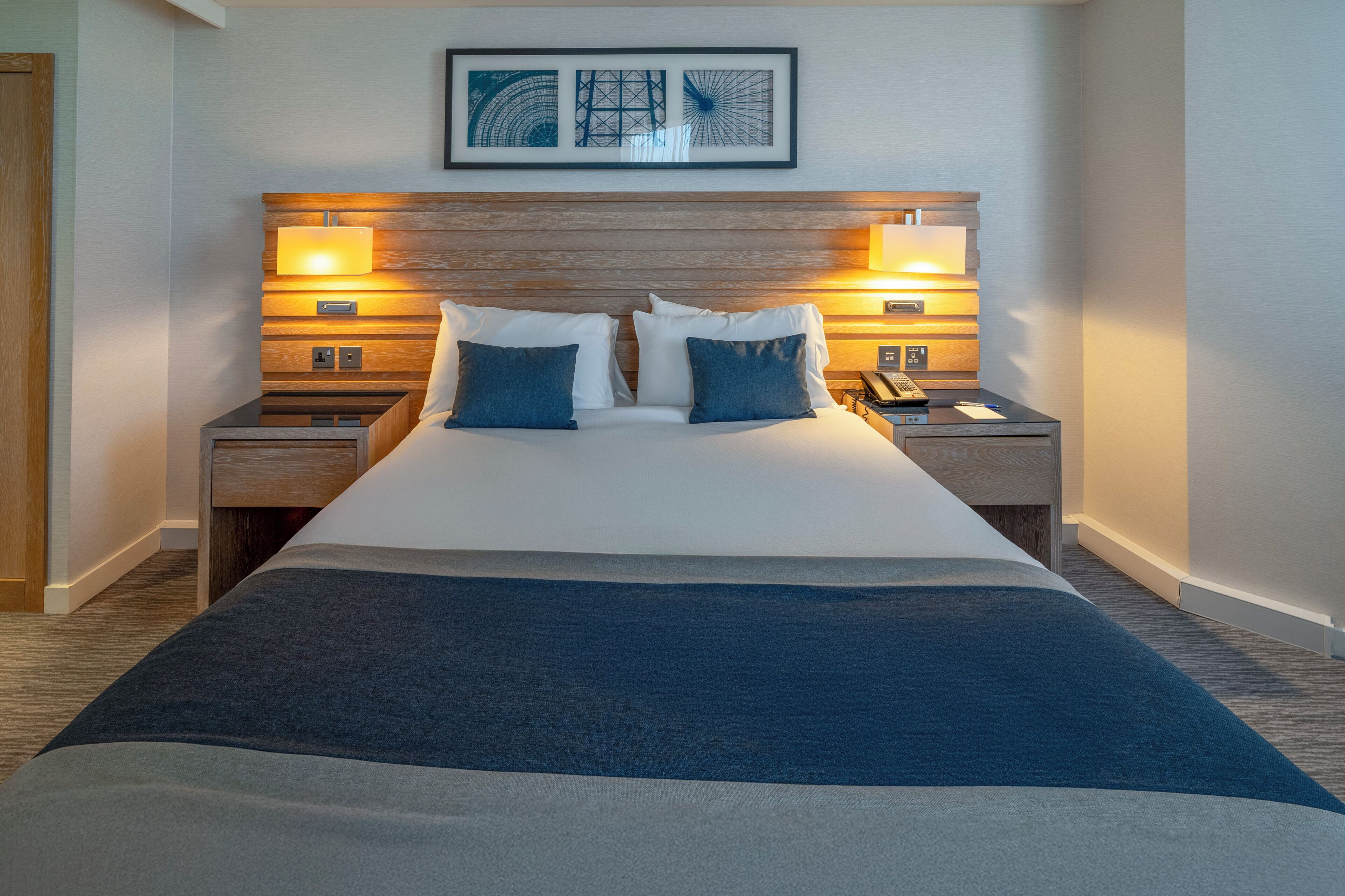 Quarto de hotel com uma cama grande, duas mesas de cabeceira, uma cabeceira e uma obra de arte na parede.