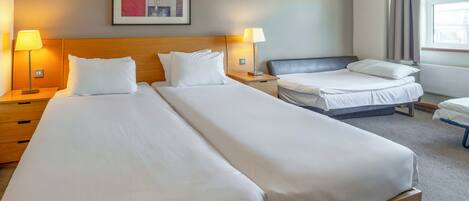 Quarto de hotel com duas camas, cabeceira de madeira, abajures, um quadro na parede e uma janela com cortinas.