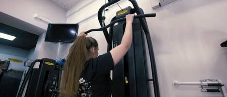 Uma academia com equipamentos de exercícios, uma televisão e um ar condicionado fixado na parede.