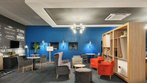 Uma área de estar moderna com uma parede azul decorativa, diversas opções de assento incluindo poltronas e pufes, uma estante de madeira e um tapete estampado.