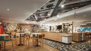 Um restaurante moderno com mesas e cadeiras de madeira, área de bar e um mural na parede.