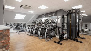 Uma academia com várias máquinas de exercício, uma parede de tijolos e teto com claraboias.
