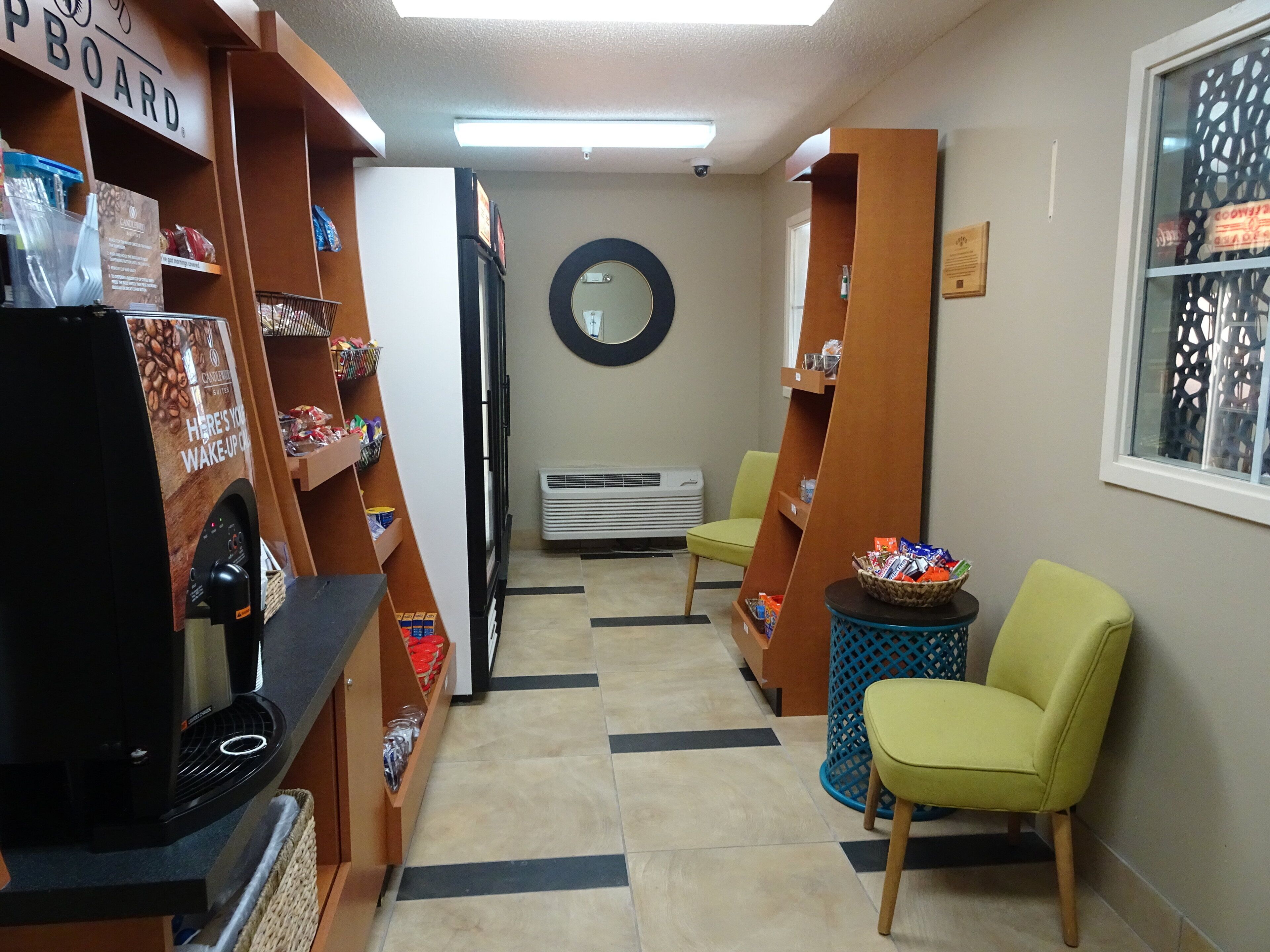 Um corredor com máquina de café, prateleiras com lanches, um espelho e uma janela com cortinas estampadas.