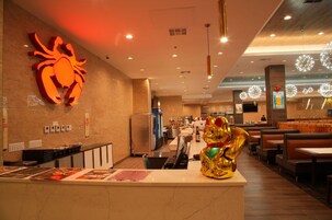 Interior de restaurante com decoração de caranguejo, estátua de gato dourado e balcão com cardápios.