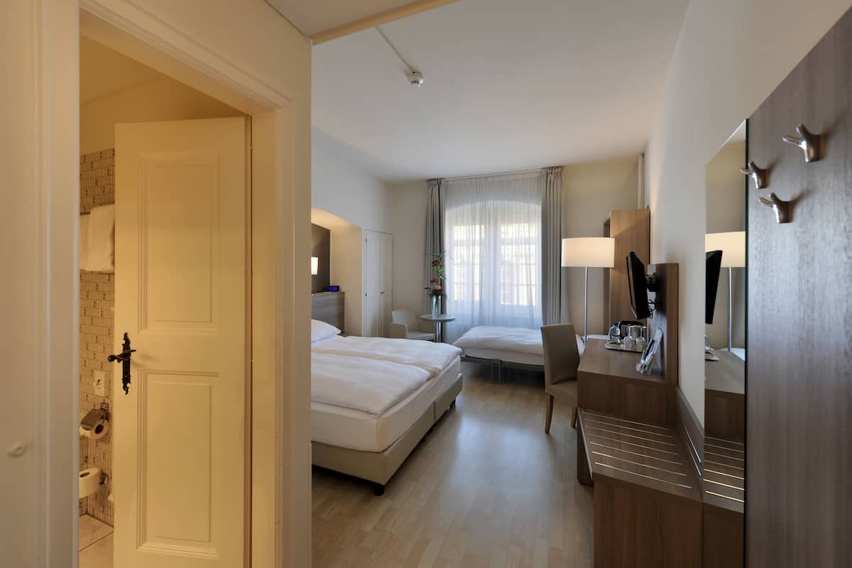Quarto de hotel com cama, mesa de cabeceira, cadeira, escrivaninha e um espelho grande.