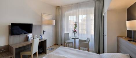 Quarto de hotel com cama, escrivaninha, televisão e duas cadeiras.
