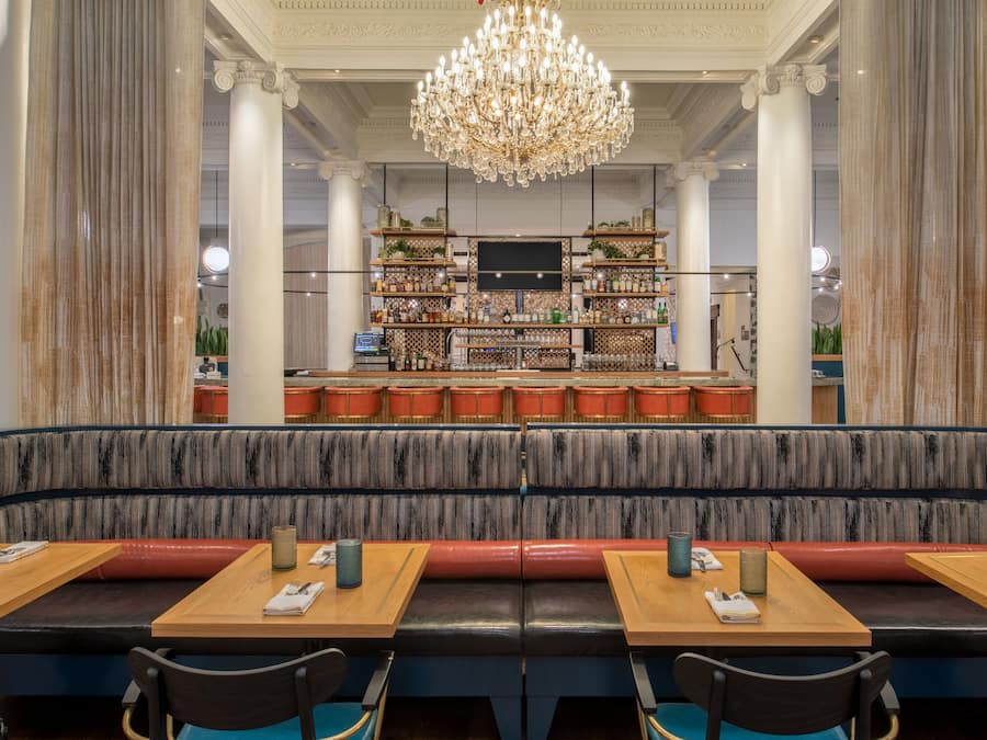Um restaurante com área de bar central, tetos altos e um candelabro.
