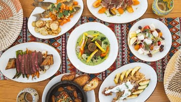 Diversos pratos em uma mesa de madeira, incluindo peixe, carne e legumes.