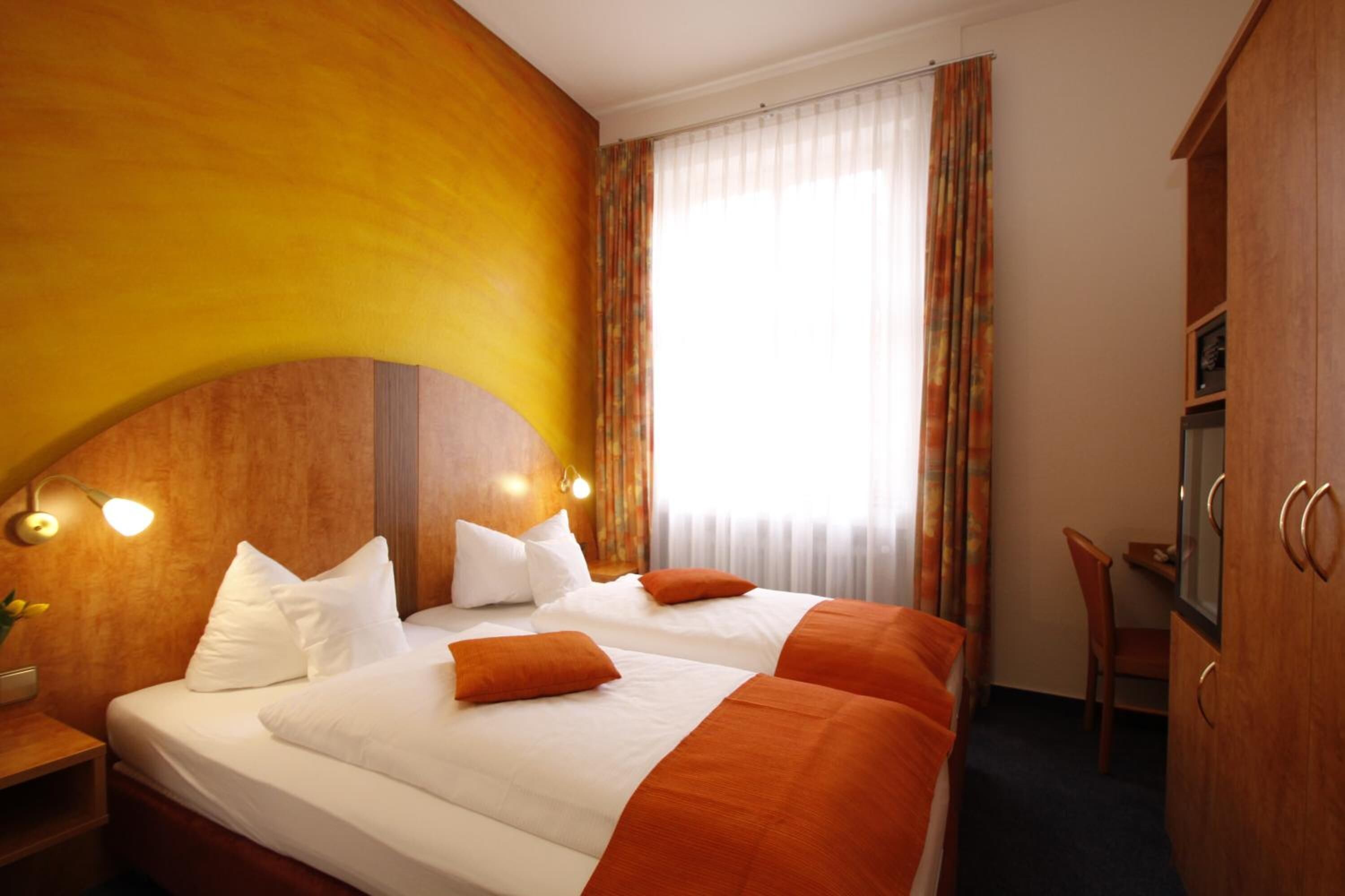 Quarto de hotel com duas camas, cabeceira de madeira, uma escrivaninha e uma cadeira.