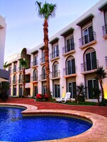Um hotel com piscina, palmeiras e um pátio com espreguiçadeiras.